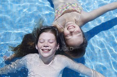 Two Girls Floating In Swimming Pool With Eyes Closed High Angle View