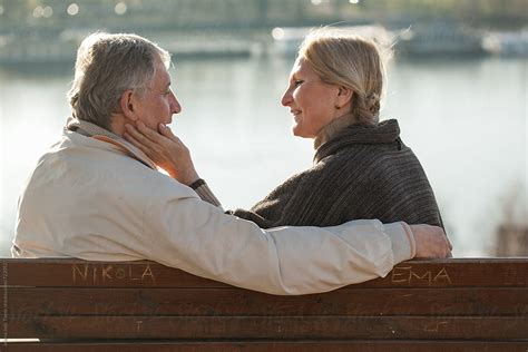 Couple In Love Sitting On A Bench Near The River By Stocksy