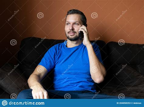 Handsome Man With A Beard Is Talking On A Cell Phone Sitting On The