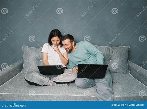Young Smiling Couple Relaxing On Sofa With Their Laptops Stock Image