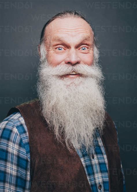 Portrait Of Smiling Senior Man With Long White Beard On Gray Background