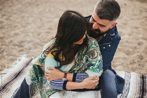 Hipster Interracial Couple Sitting On Blanket On Beach Hugging By