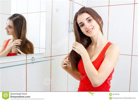 Cute Young Girl Stands In The Bathroom Smiling And Touching Her Hair