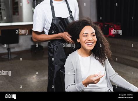 Cheerful African American Client Sitting Near Hairdresser In Apron