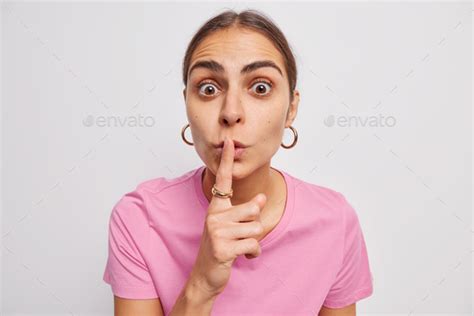 Portrait Of Surprised Adult Woman Presses Index Finger To Lips Shows