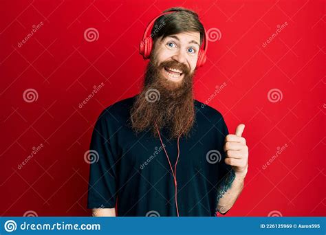 Redhead Man With Long Beard Listening To Music Using Headphones Smiling