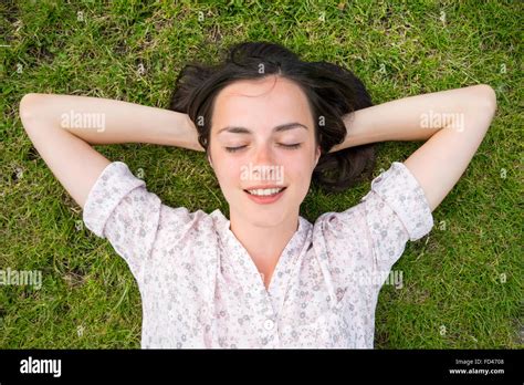 Beautiful Young Woman Relaxing On Green Grass With Hands Under Head And
