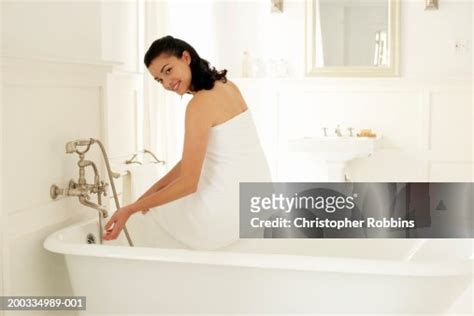 Young Woman Sitting On Edge Of Bath Testing Water With Hand Portrait