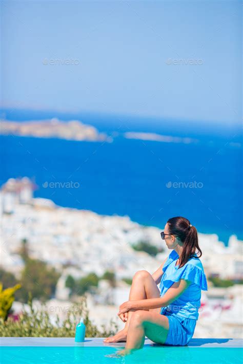 Slim Woman Applying Sunscreen On Her Legs Sitting On The Edge Of Pool