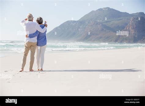 Rear View Of A Couple Standing With Arm Around Each Other On The Beach