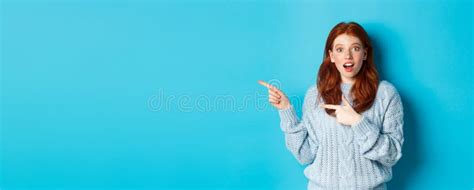 Amazed Redhead Girl In Sweater Pointing Fingers Left At Logo And