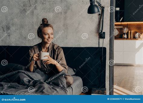 Joyful Happy Smiling Caucasian Female In Satin Cozy Pajama Holding Cup