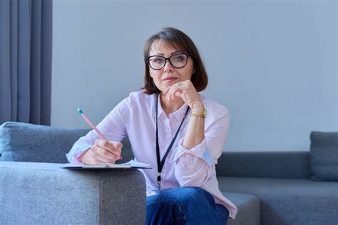 Portrait Of Middle Aged Female Therapist With Clipboard In Office Stock