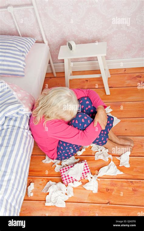 Sad Woman With Pink Pajama And Tissues Sitting On Floor Against Bed