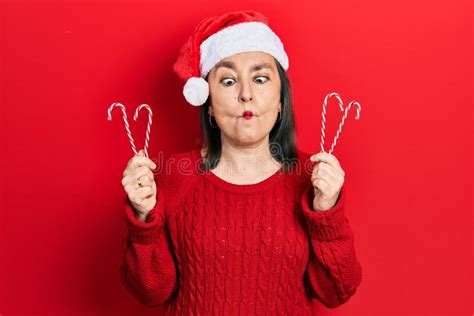 Middle Age Hispanic Woman Wearing Christmas Hat Holding Candy Making