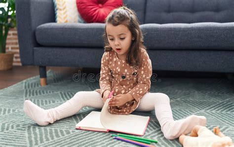 Adorable Hispanic Girl Sitting On Floor Drawing On Notebook At Home
