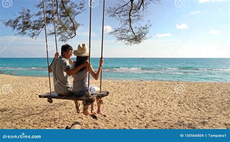 Happy Asian Couple Swinging On A Swing At The Beach During Travel Trip