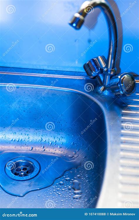 A Stream Of Clean Water Flows Into The Stainless Steel Sink In Blue