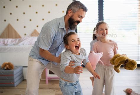 Father With Three Daughters Indoors At Home Having Fun Playing Stock
