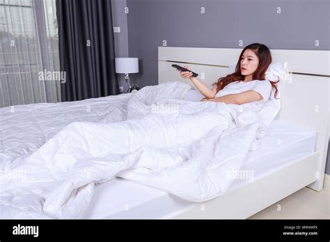 Woman Lying On A Bed With Remote Control And Watching Television In The