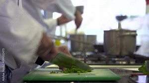 Cutting parsley in restaurant kitchen. A cook in the background stirs in a pan.