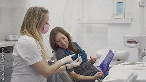 Orthodontists explains to woman patient about teeth alignment procedure. Female doctor or dentist shows a patient a brochure or booklet about dental medical procedure for braces or invisible retainer