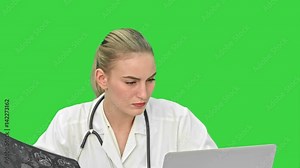 Young female doctor examining xray writing down results diagnosis to laptop computer on a Green Screen, Chroma Key.