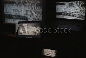 Four digital computer device screens displaying a choppy static noise pattern in a dark room.