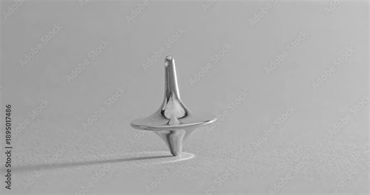 Metallic Spinning Top Falling Over. Linear footage of a shiny chrome top in steady rotation, progressively wobbling with increasing tilt until it fully topples on a matte gray surface.
