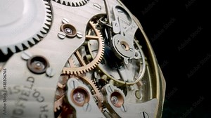 Macro shot of the internal parts of antique pocket watch. Clockwork with rotating spring, gears, cogwheel and wheels with tootheds on isolated black studio background. Disassembled silver watch.