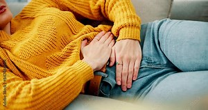 Woman, hands and tummy ache with pain or cramp on sofa in menstruation, constipation or gastro at home. Closeup of female person with diarrhea, abdomen injury or digestion issue from stomach virus