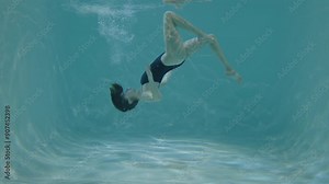 Graceful flexible attractive sportswomen exercising artistic swimming skills, stretching in upside down pigeon position underwater while training in swimming pool.