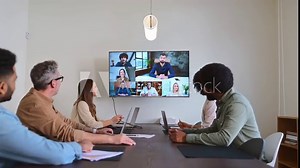 A team of professionals engaged in a productive video conference, combining in-person and remote participants on a large screen in a conference room. Effective communication tools in achieving goals