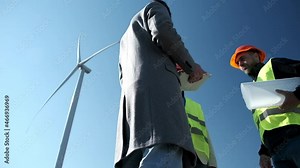Wind turbines produce alternative energy. Experienced engineers and chief architect with tablet adjust parameters of wind turbines low angle shot