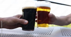 People with beer toast in pub. Dark and light delicious beer in a glass