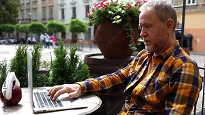 Handsome adult mature business man using laptop outside enjoying sunny beautiful day resting in cafe outdoor. Internet connecting. Communicating online chat app. Traveling modern urban lifestyle.