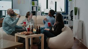 Multi ethnic group of colleagues having fun after work at office. Workmates enjoying after hours celebration with bottles of beer, drinks, pizza, and snacks. Coworkers laughing