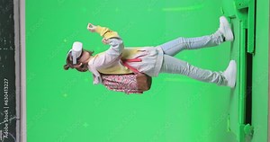 Vertical shot on green screen background. VR or AR online walk. Girl in augmented reality googles walks through virtual world and clicks invisible virtual buttons. Walking on a treadmill side view.