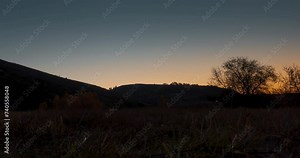 4k Mountain meadow time-lapse at the summer or autumn sunrise time. Wild nature and rural field. Clear sky, trees, green and yellow grass, sun rays on horizont. Motorised slider movement.
