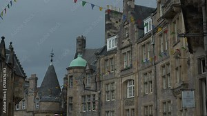 Charming stone facades of old townhouses with strung chains of colorful flags. Brightly colored bunting flags flutter in wind across the street in medieval city centre. Festive mood in historic town.