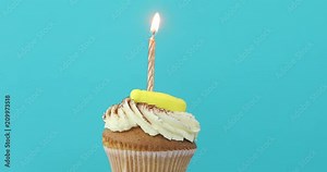 Birthday cupcake with a single yellow candle over a blue background