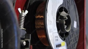 Welding wire spool turning as reflections of sparks are seen. This is a Wire feed welder using copper wire.