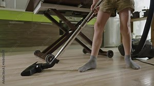 Little child helps his parents in housework, cleaning the floor using a vacuum cleaner in the kitchen. Children's household duties