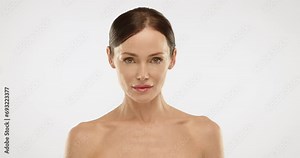 Beautiful woman looking into the camera with attractive facial features and a charming smile. She takes care of her appearance and hair. Photo model on a light background. Health and beauty. 4K