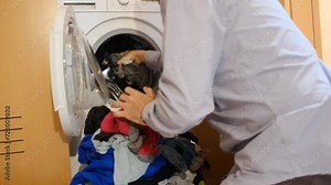 Man putting the clothes washer putting dirty clothes and taking out clean clothes, mechanical washing machine. Gender equality, responsibility, domestic chores, men, women, helping the family