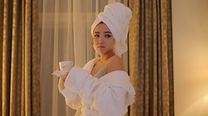 Stress relax self-isolation at home. asian girl in the bedroom holds hot drink in hands. A towel is tied around the head. The girl is looking at the camera. Mental comfort.