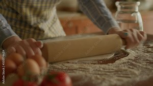 Young adult woman rolling dough standing in the kitchen. Female chef in apron baking pizza at home. Handheld camera.