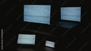 A side angle shot of four digital computer device screens displaying a choppy static noise pattern in a dark room.