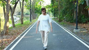 Healthy asian senior woman standing upright doing swinging their arms up and down while walking exercising outdoor on the street,female elderly workout by stepping and stretching arms alone at the par