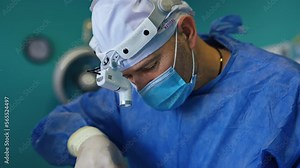 Focused busy surgeon with flashlight on head applying metal tools. Portrait of a medical professional carrying out surgery.